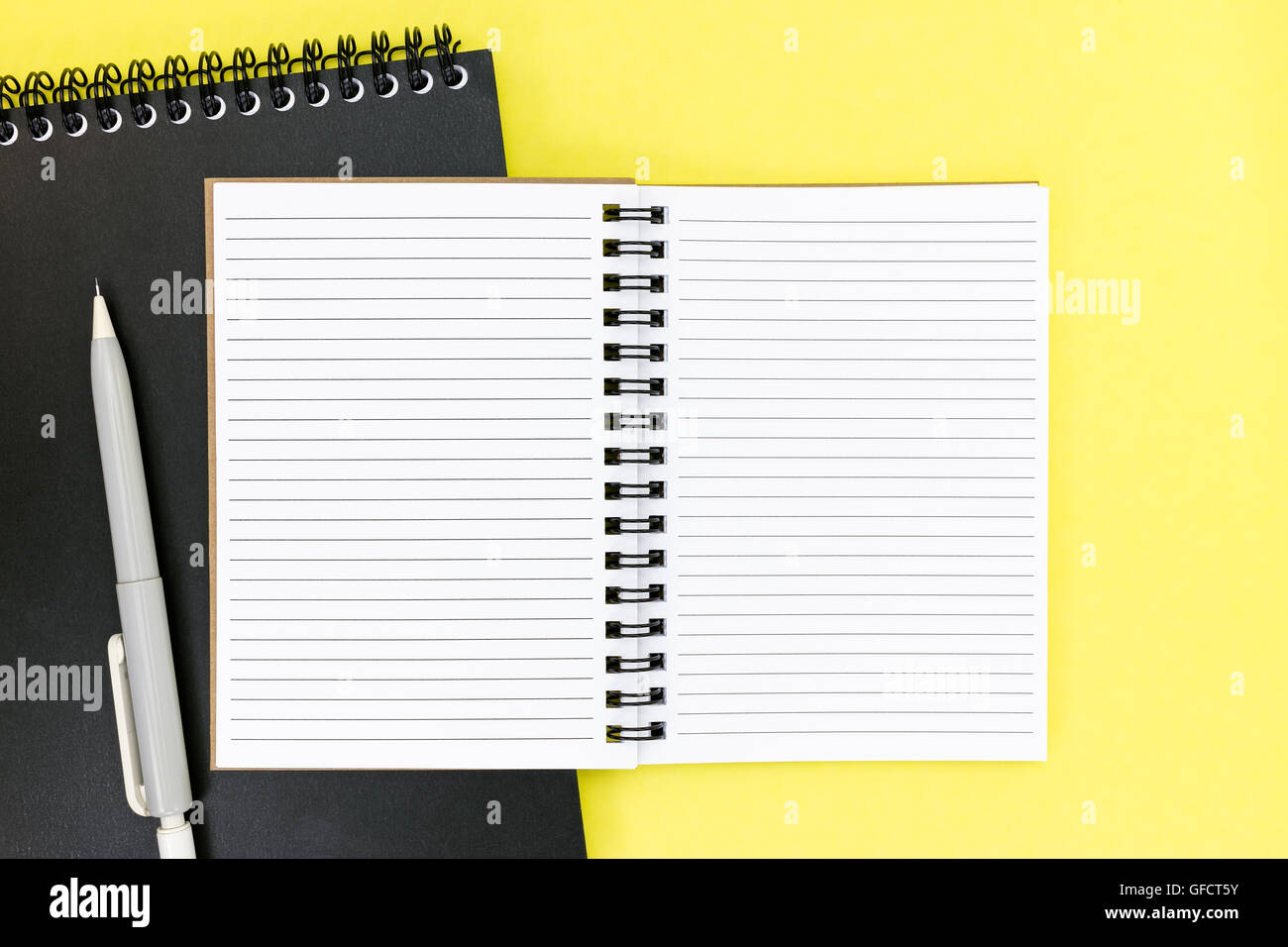 open spiral notebook, black notepad and mechanical pencil on yellow ...