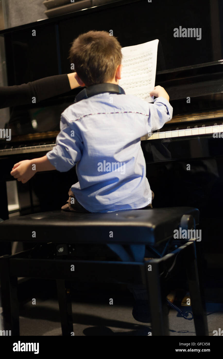 Rear view of a little boy learning piano from instructorcolor image ...