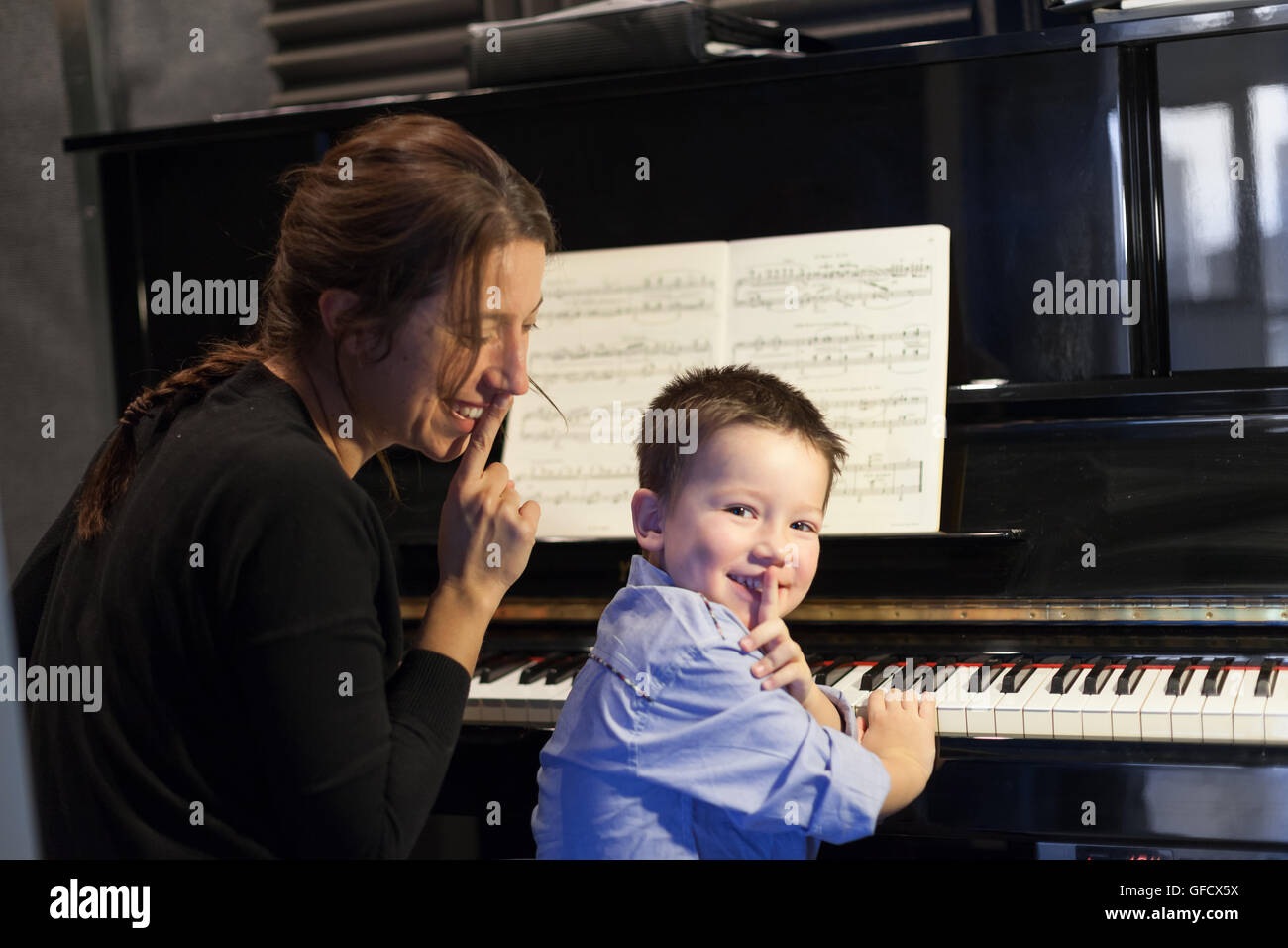 Boy putting index finger on lips with his piano instructor and ...
