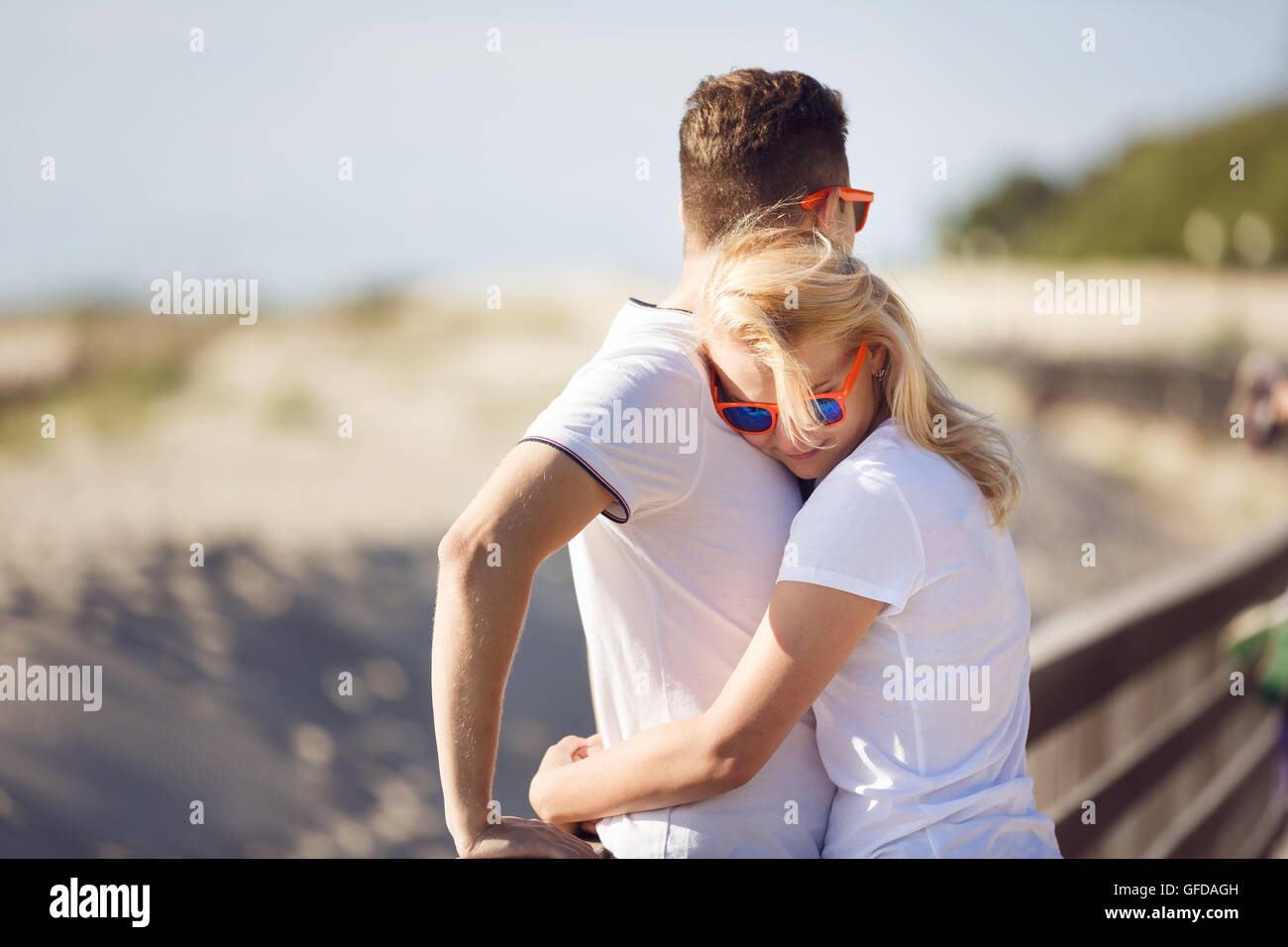 Young couple are hugging by the wooden fence on the beach, summer time ...