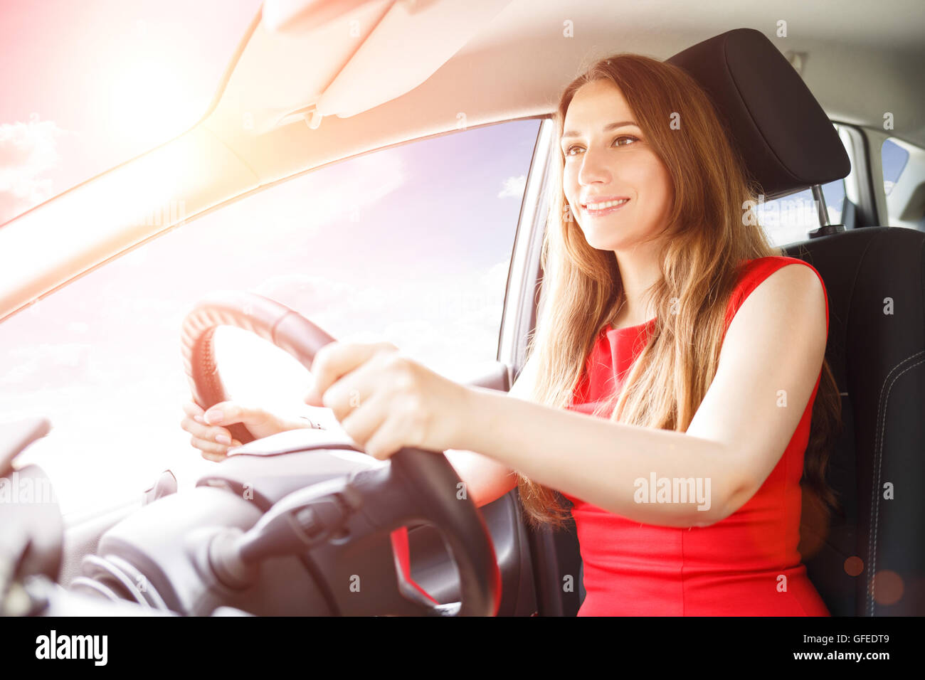 Young lady in red dress driving a car with sunbeams coming through the ...