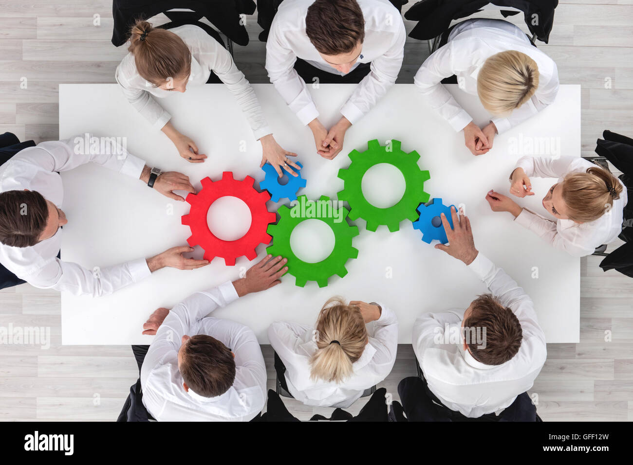 Business team sitting around the table with cogs, teamwork concept ...