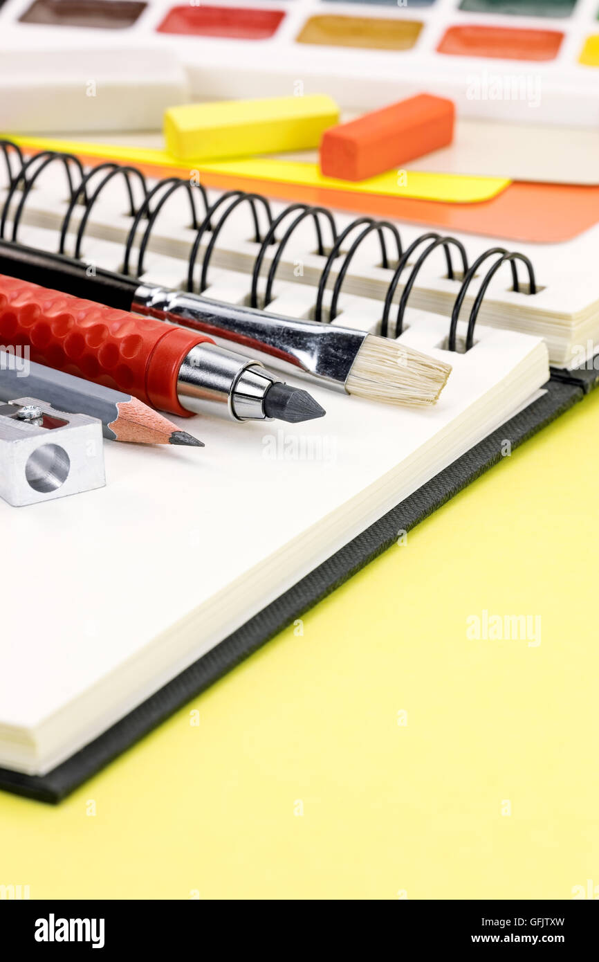 notebook with pencils, crayons and paintbrush on yellow desk background ...
