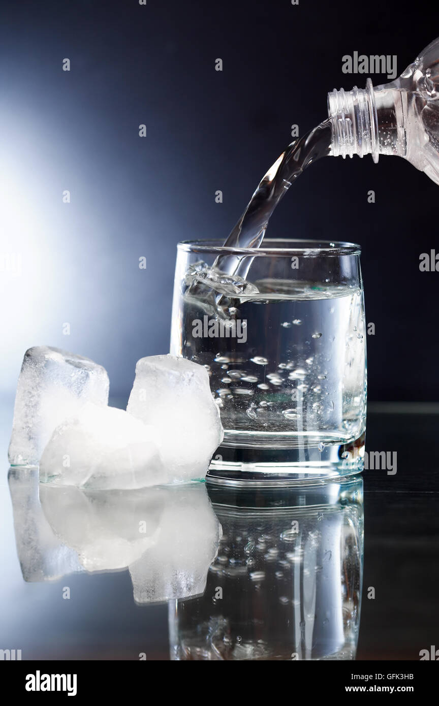 Mineral water flowing from bottle to glass near ice cubes on dark background Stock Photo - Alamy