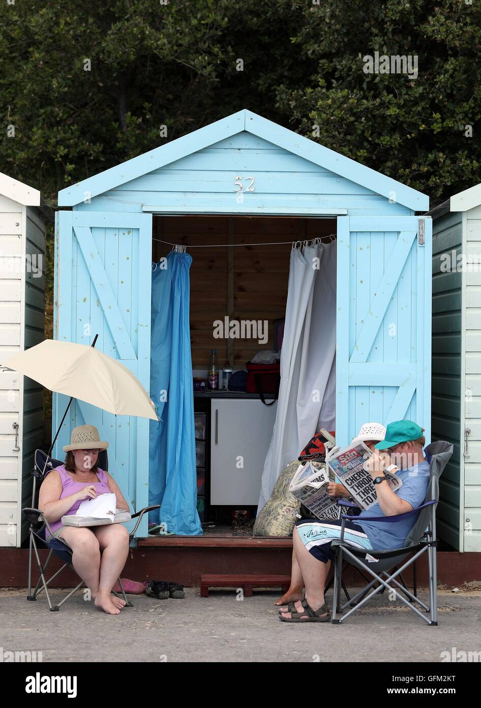 People sit outside beach huts on Avon Beach in Mudeford, Dorset Stock ...