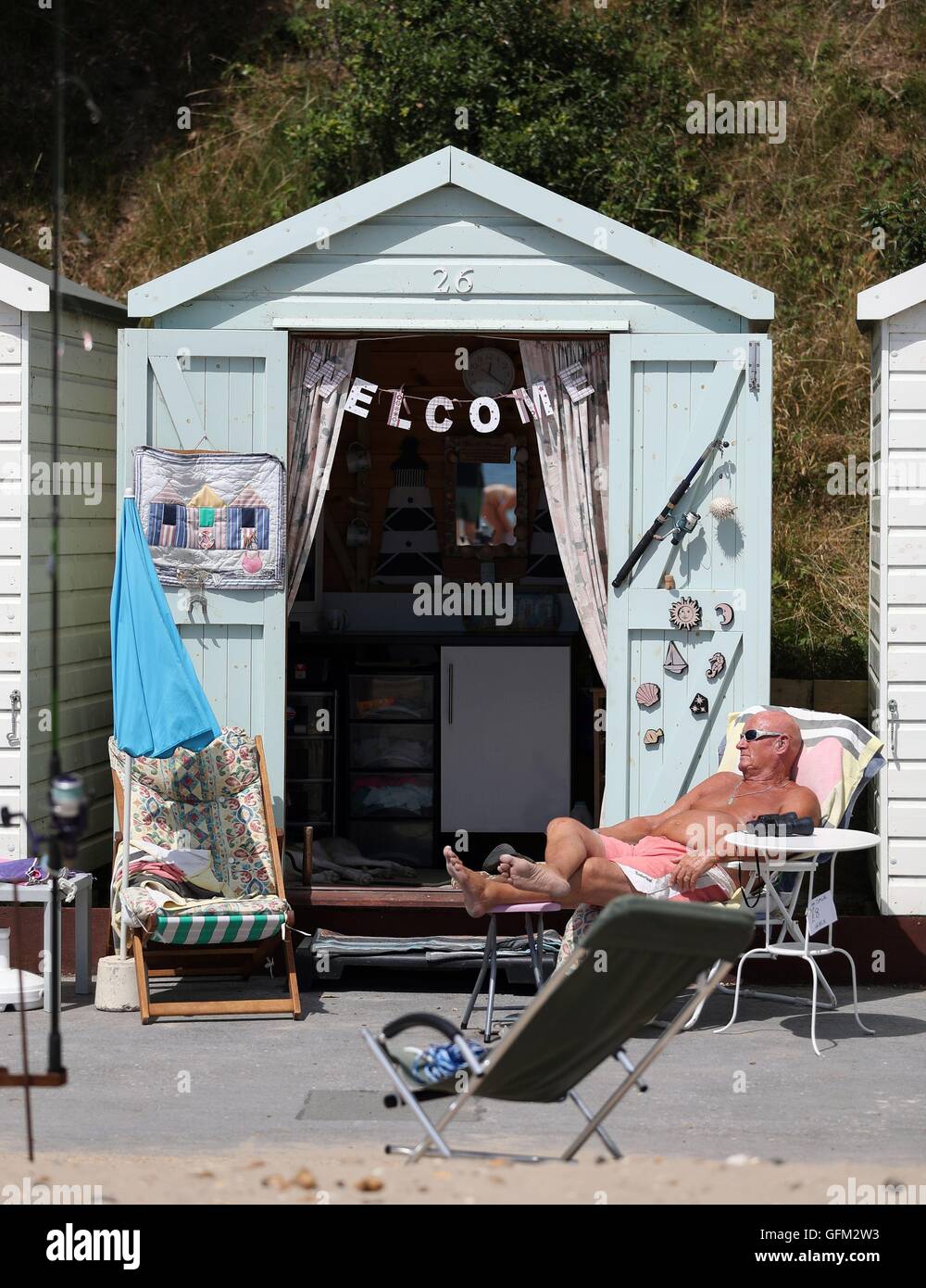 People sit outside beach huts on Avon Beach in Mudeford, Dorset Stock ...