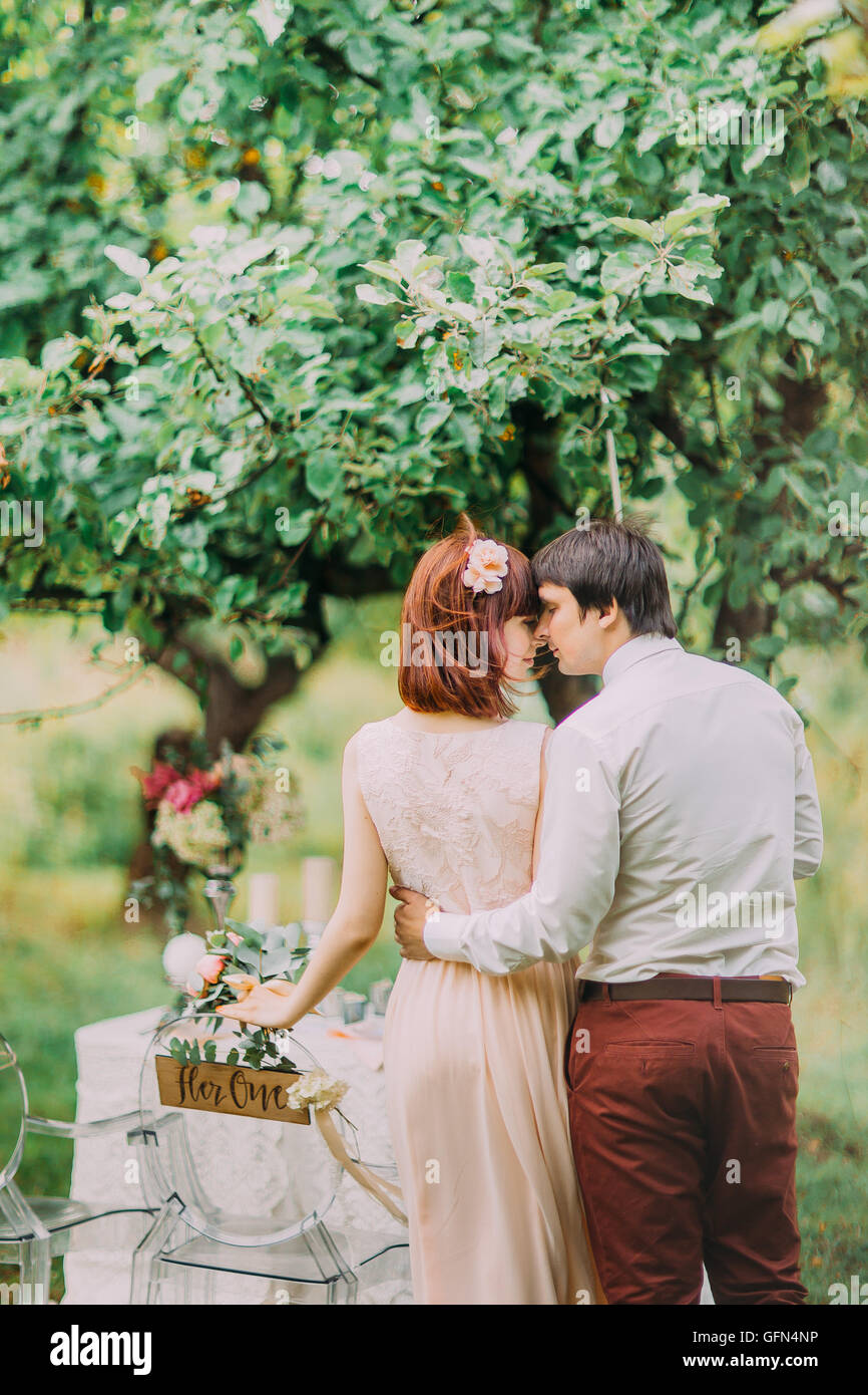Bride and groom posing at decorated banquet table in the summer park ...