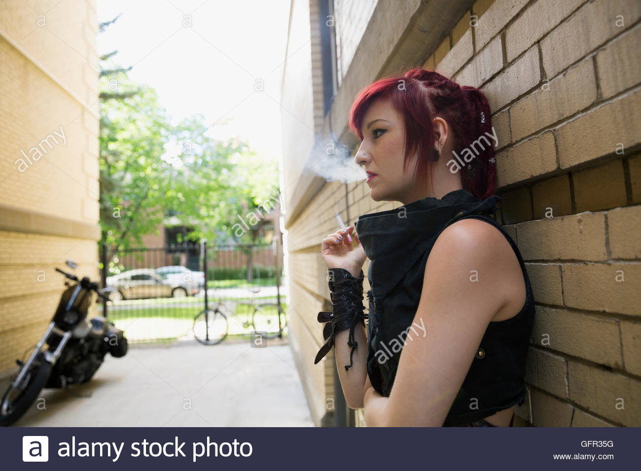 Cool woman with red hair smoking cigarette in urban alley Stock Photo ...