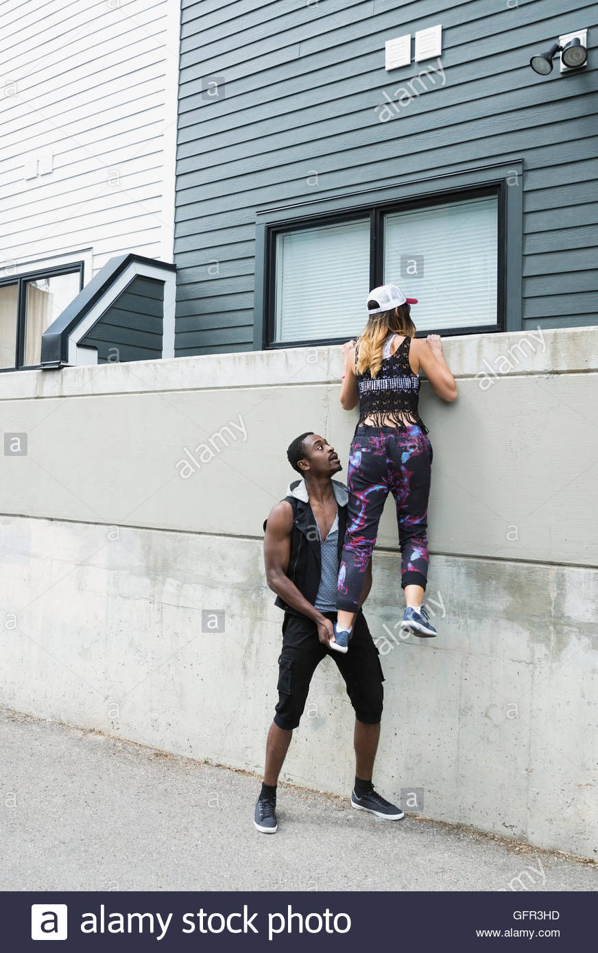 Young man lifting young woman over urban wall Stock Photo - Alamy