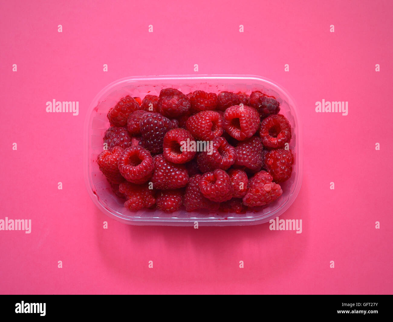 Fresh raspberries in plastic box on a pink background Stock Photo - Alamy
