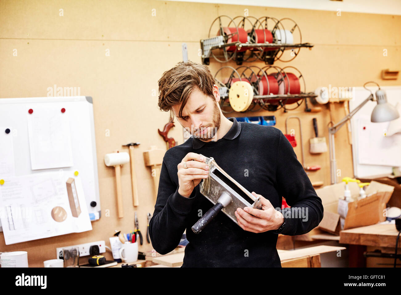 A furniture workshop A young man holding an object and examining it ...