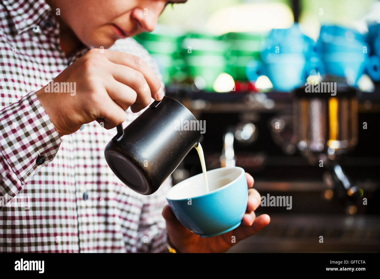 A man pouring hot milk into a cup of coffee to make a pattern on the ...
