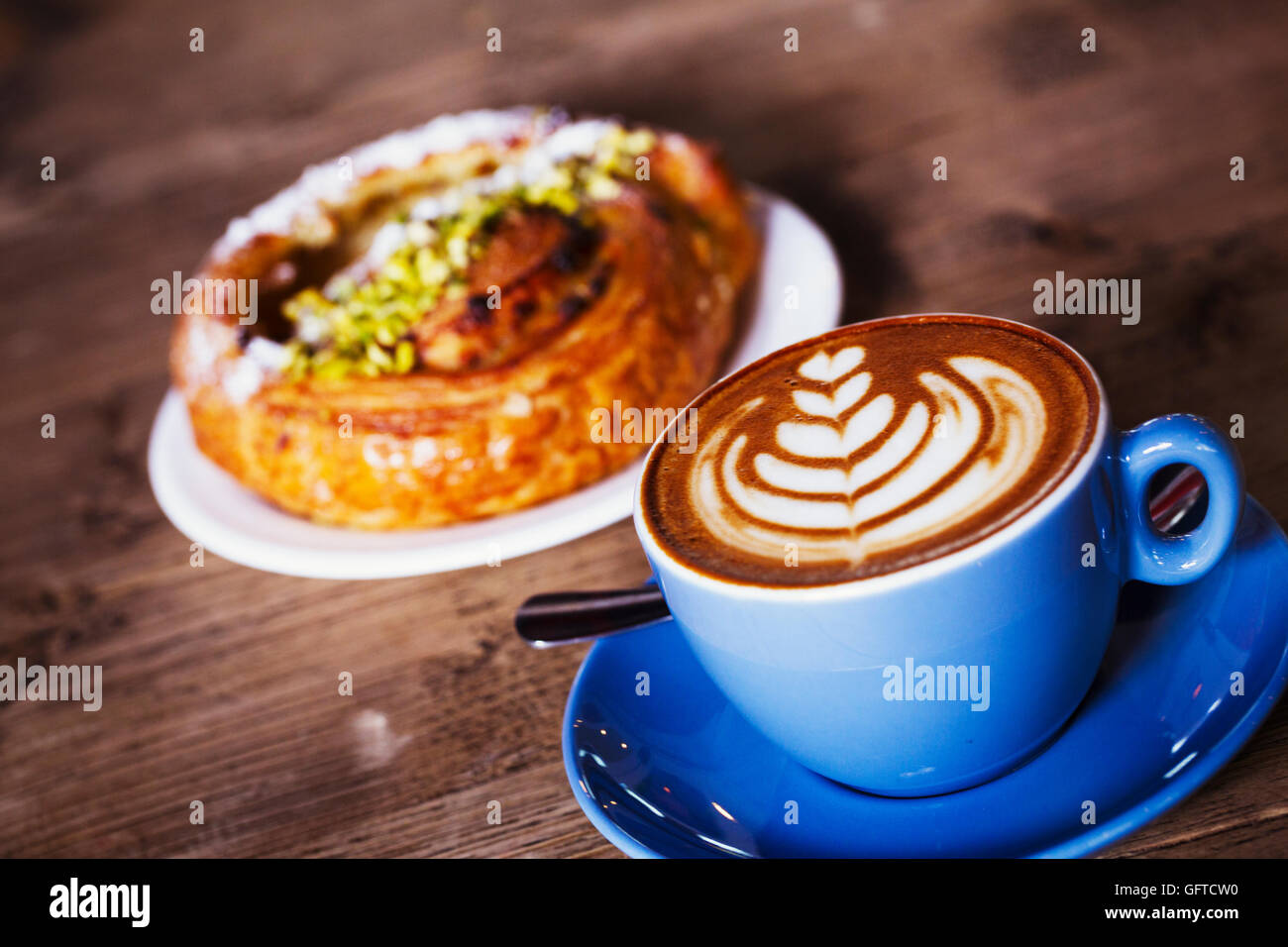 A cup of coffee with a fern leaf pattern in the froth and a croissant ...