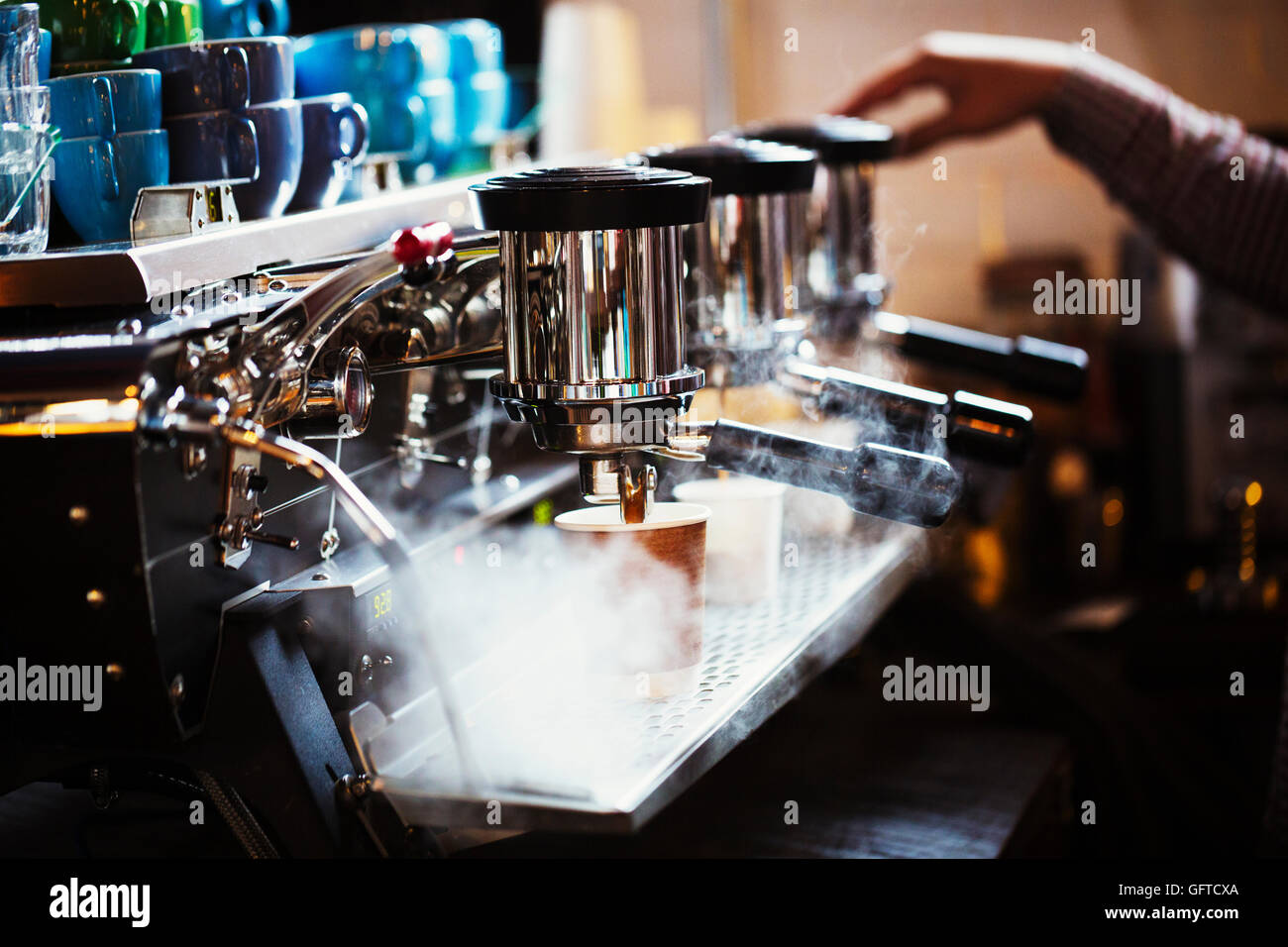 A person working at a large coffee machine with three percolating ...