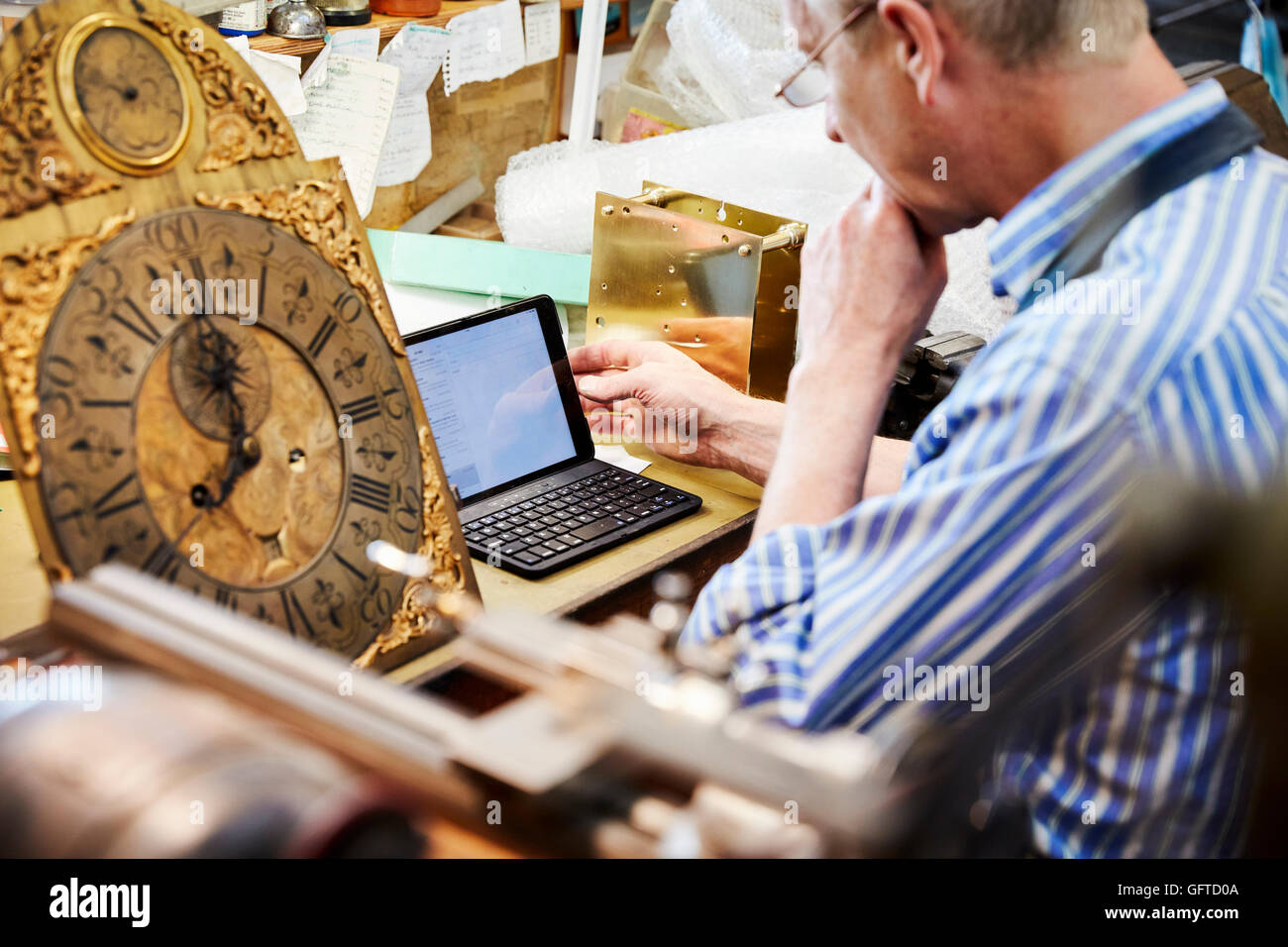 A clock maker in his workshop using a laptop Stock Photo - Alamy