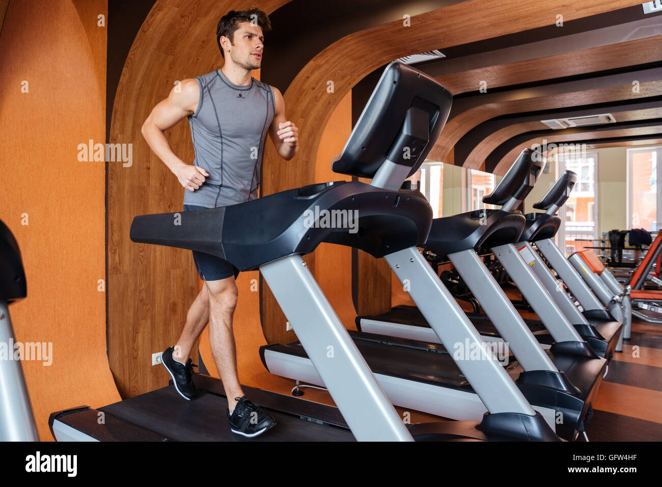 Attractive young fitness man working out and running on treadmill in ...