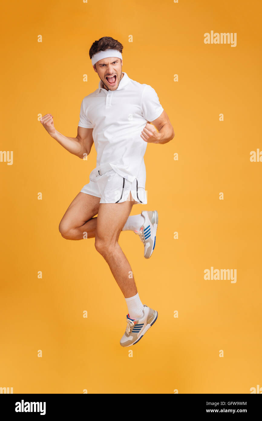 Happy handsome young sportsman shouting and jumping in the air over ...