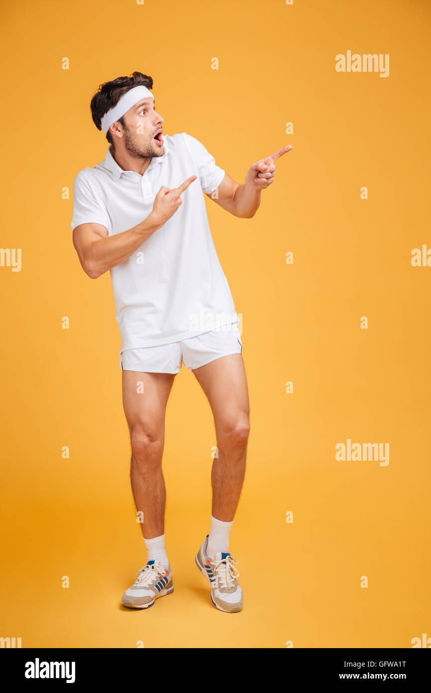 Shocked astonished young sportsman pointing away with both hands over ...