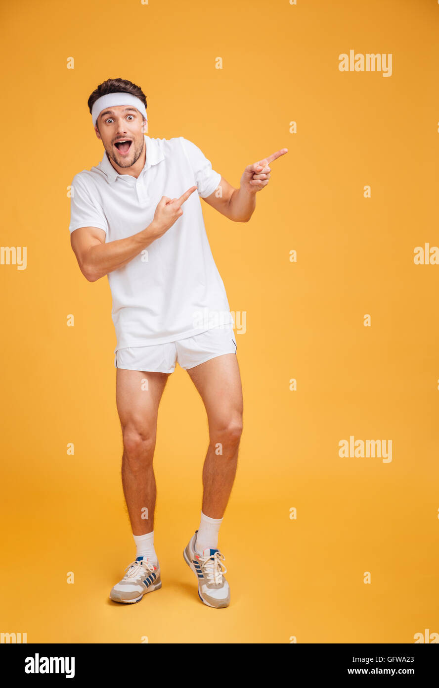Wondered surprised young man athlete standing and pointing away with ...