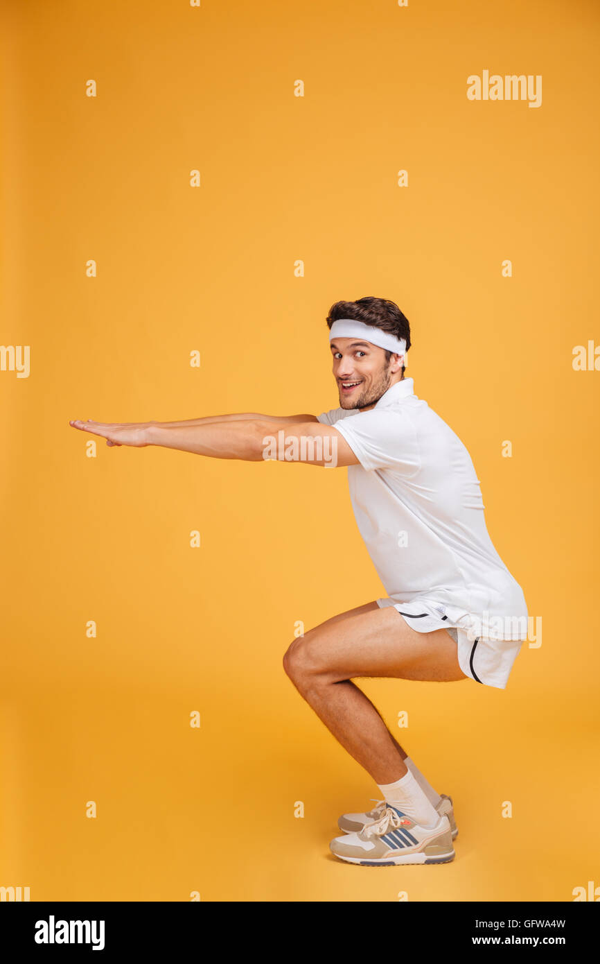 Smiling young man athlete doing exercises and working out over yellow ...