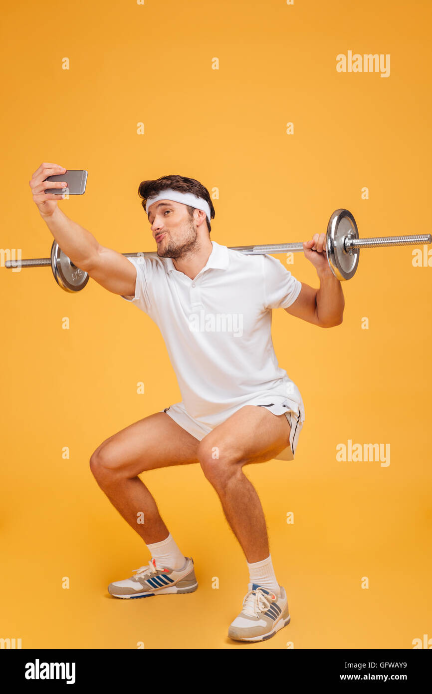 Funny young sportsman exercising with barbell and talking selfie using ...