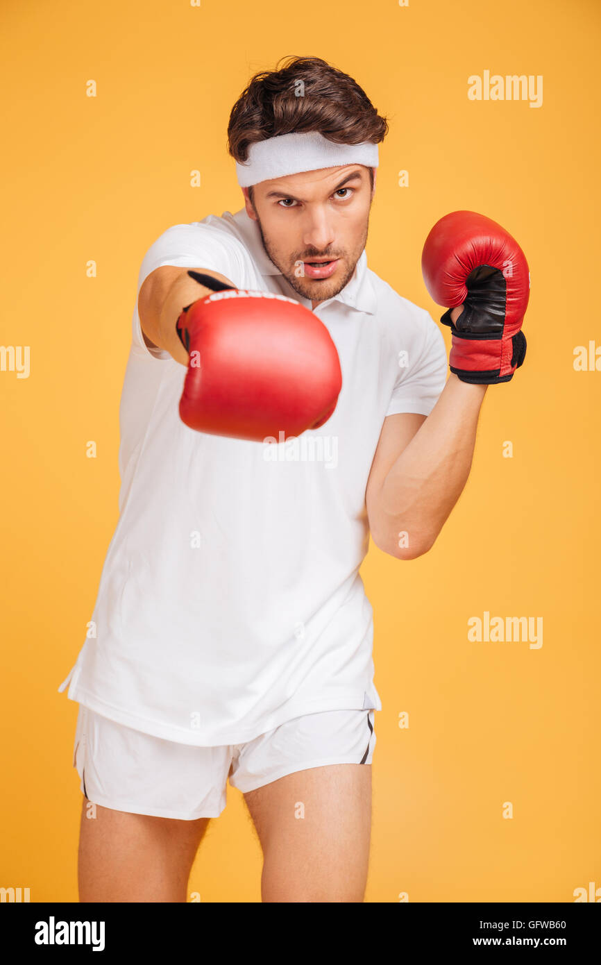 Handsome young man boxer in red gloves standing and boxing over yellow ...