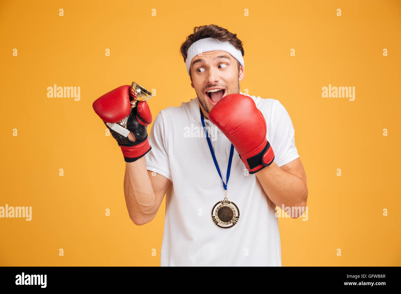 Happy excited young man boxer in red gloves with trophy cup and medal ...