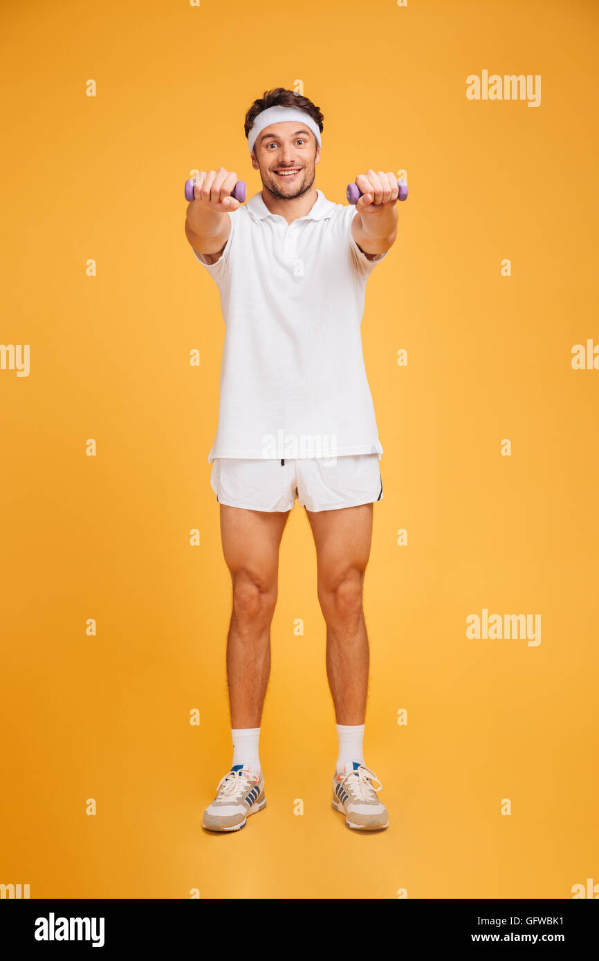 Cheerful young fitness man standing and doing exercises with dumbbells ...