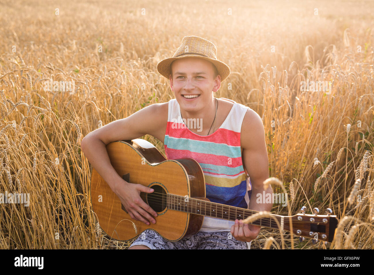 Cheerful traveling musician with his guitar outside in a wheat field ...