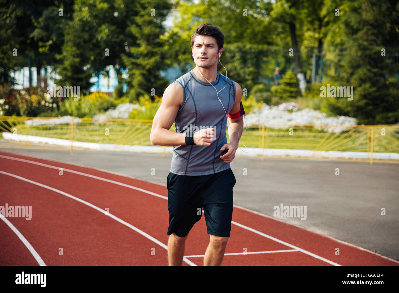 Young handsome sports man running down stadium track with earphones ...