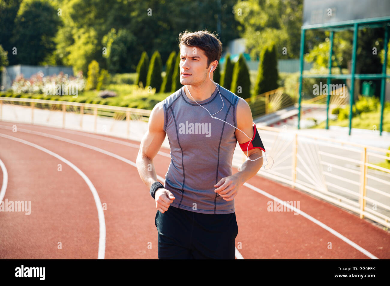 Young handsome sports man running down stadium track with earphones ...