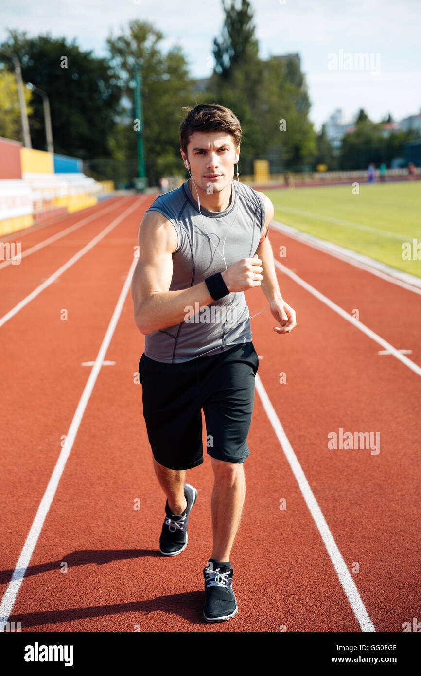 Young handsome concentrated sports man running down stadium track with ...