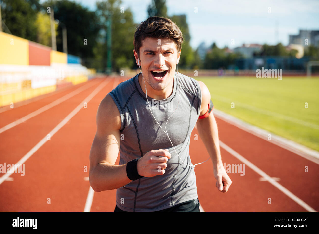 Portrait of a sports man running with earphones and shouting at camera ...