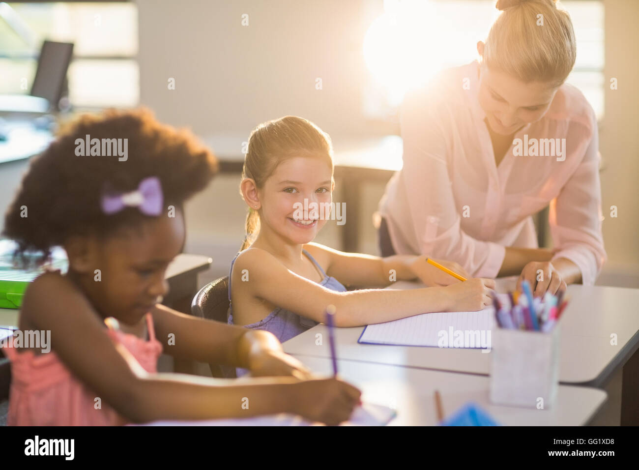 Teacher helping kids with their homework in classroom Stock Photo - Alamy