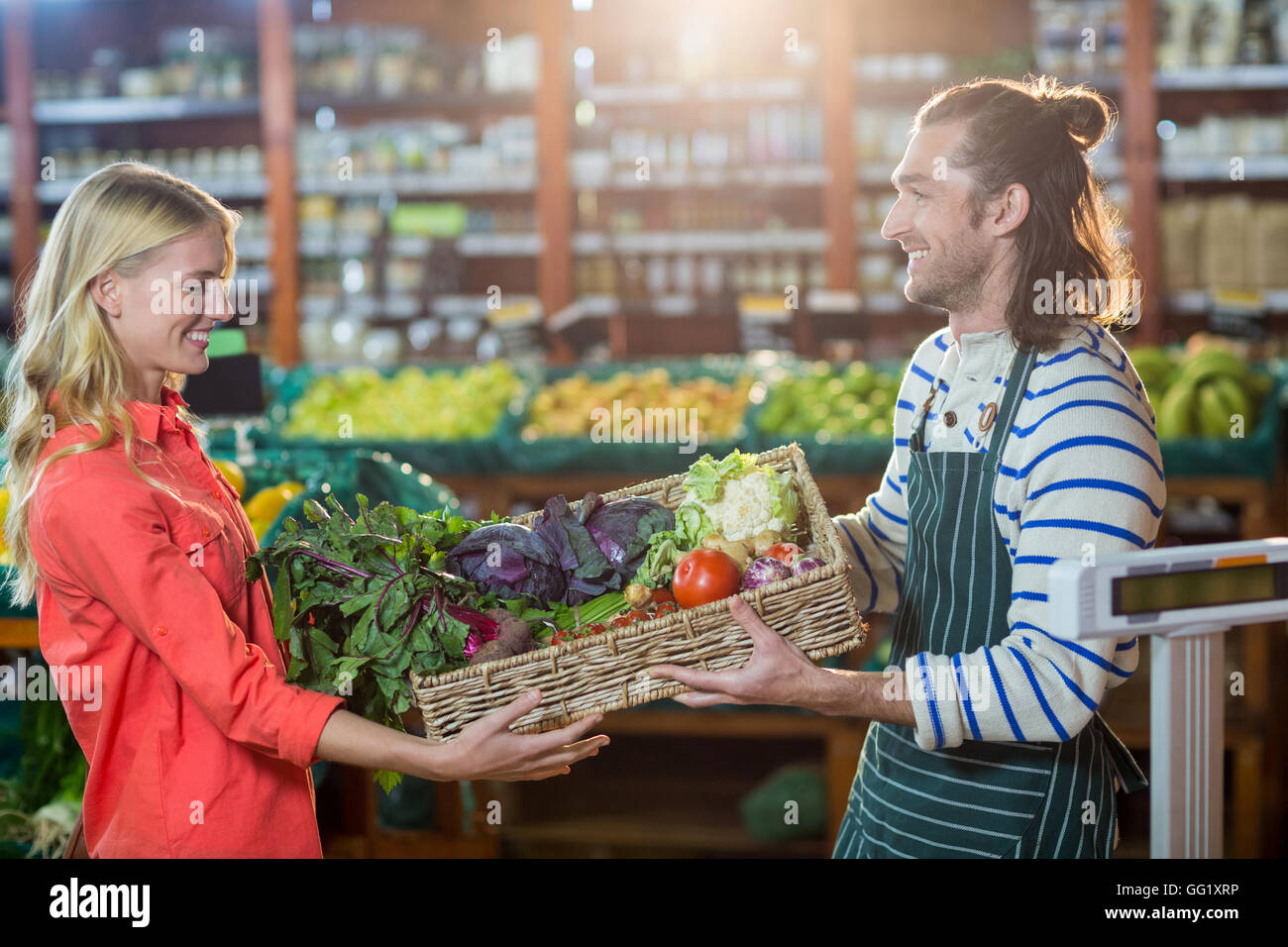 Male staff giving a crate of fresh vegetables to woman in organic ...