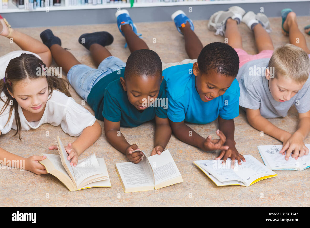School kids lying on floor reading book in library Stock Photo - Alamy