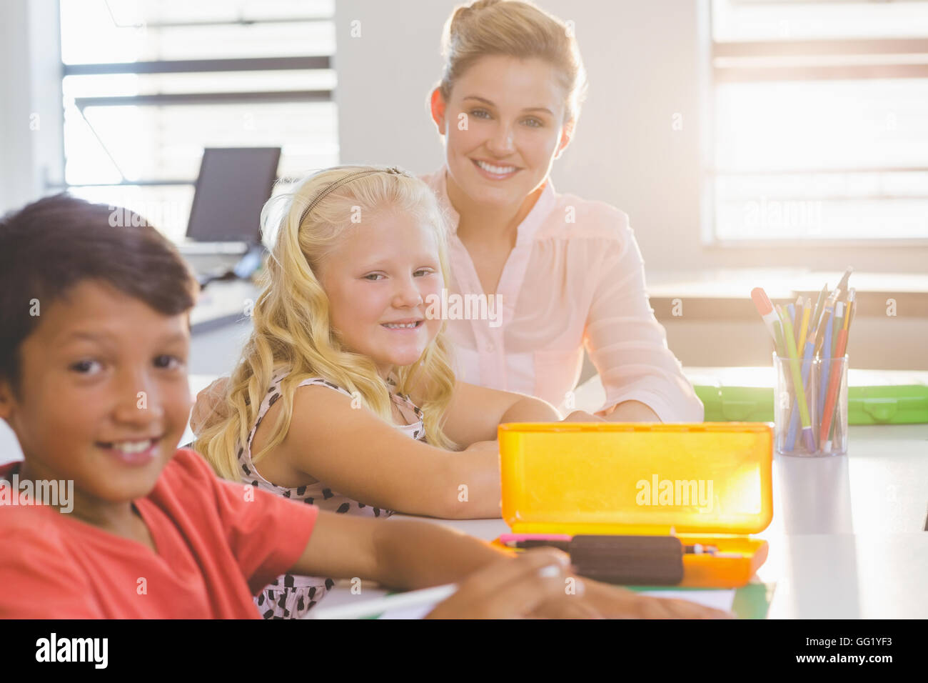 Teacher helping kids with their homework in classroom Stock Photo - Alamy