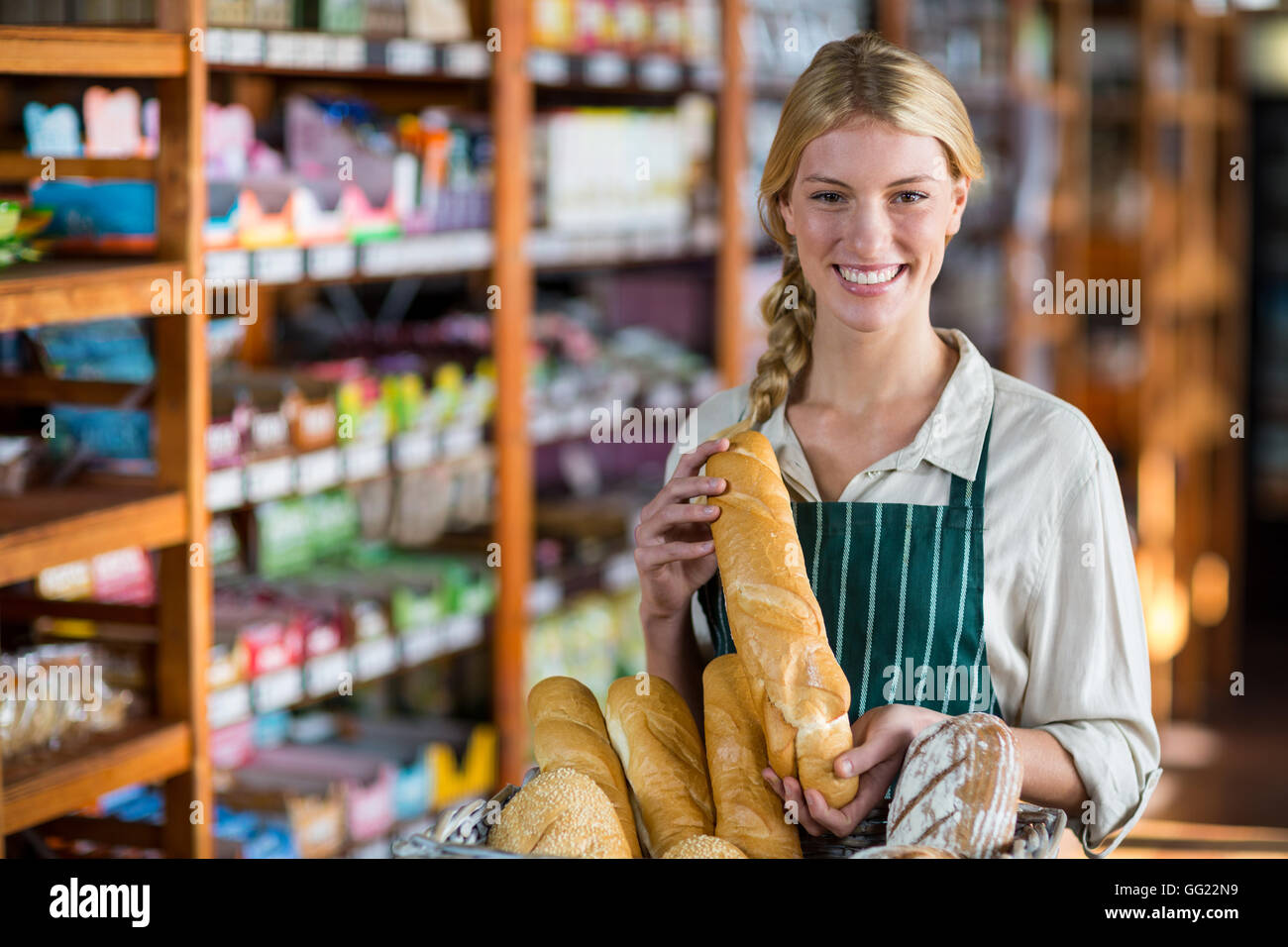 Smiling female staff holding loaf of bread at bread counter Stock Photo ...