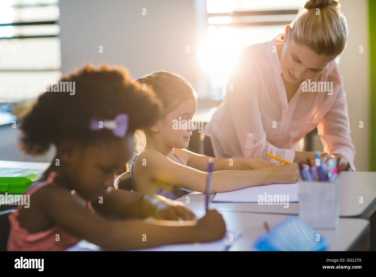 Teacher helping kids with their homework in classroom Stock Photo - Alamy