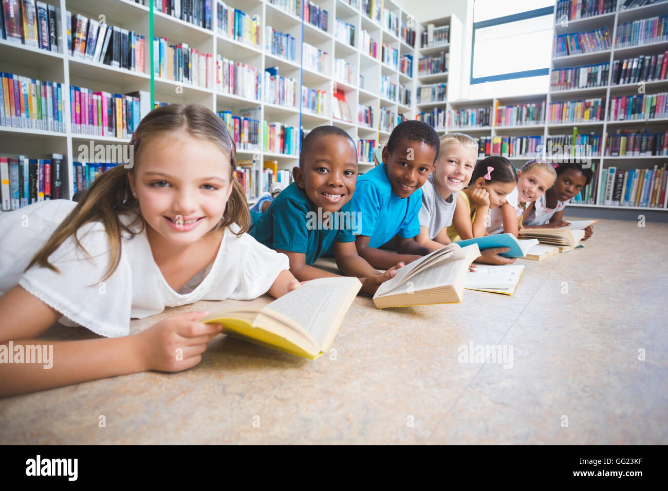 Smiling school kids lying on floor reading book in library Stock Photo ...