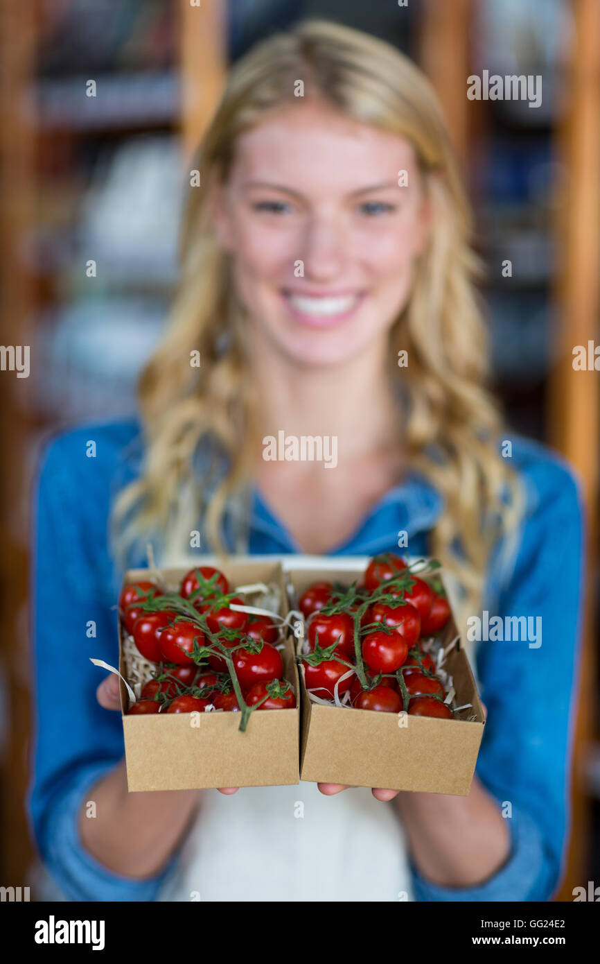 Smiling female staff holding box of cherry tomato in super market Stock ...