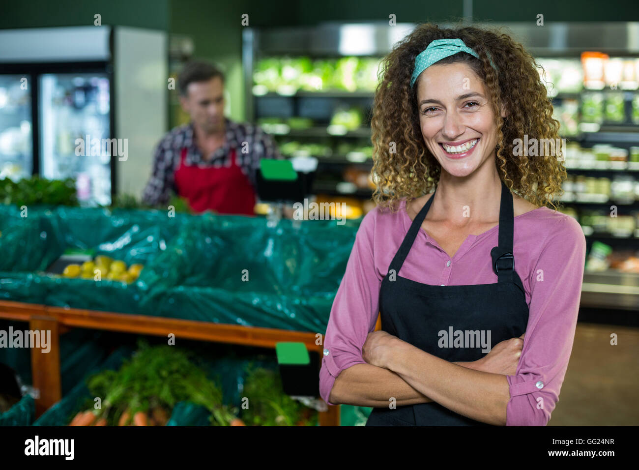 Smiling female staff standing with arms crossed in organic section ...