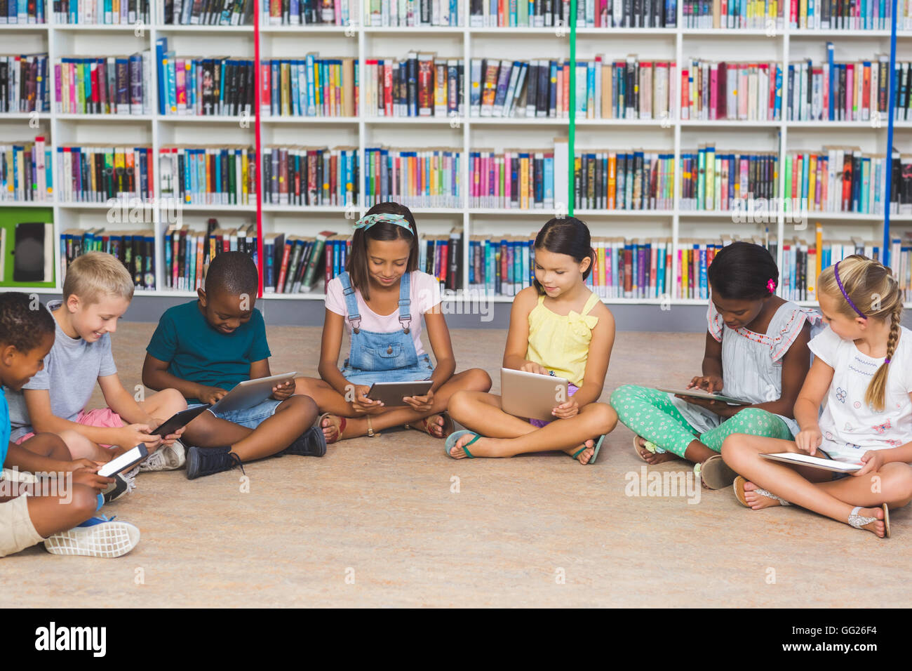 School kids sitting on floor using digital tablet in library Stock ...