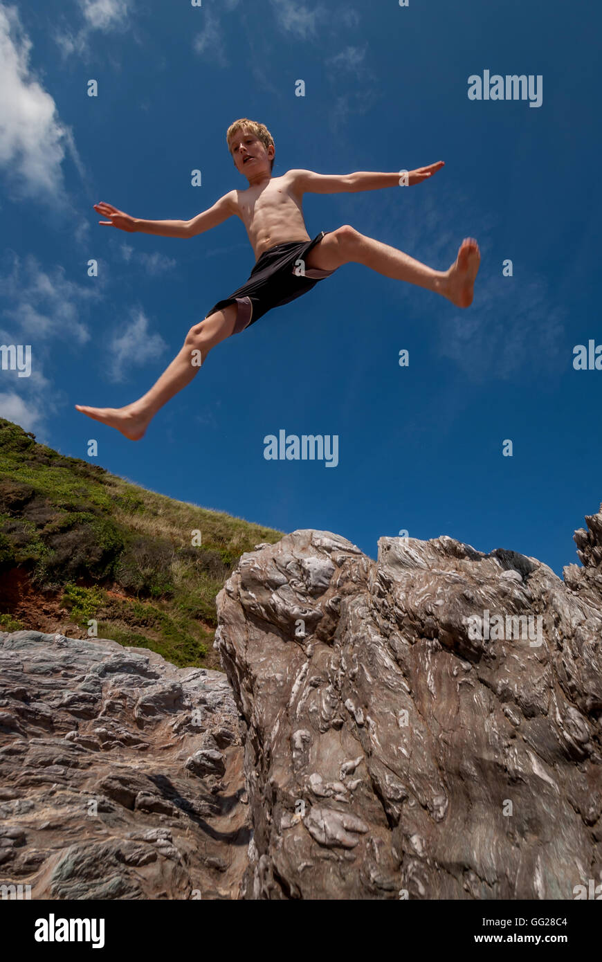 A boy jumping from rocks onto the beach in south Devon Stock Photo - Alamy