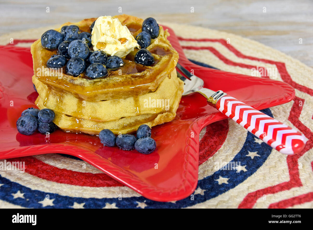 Waffle stack with blueberries and dripping syrup on red star plate ...