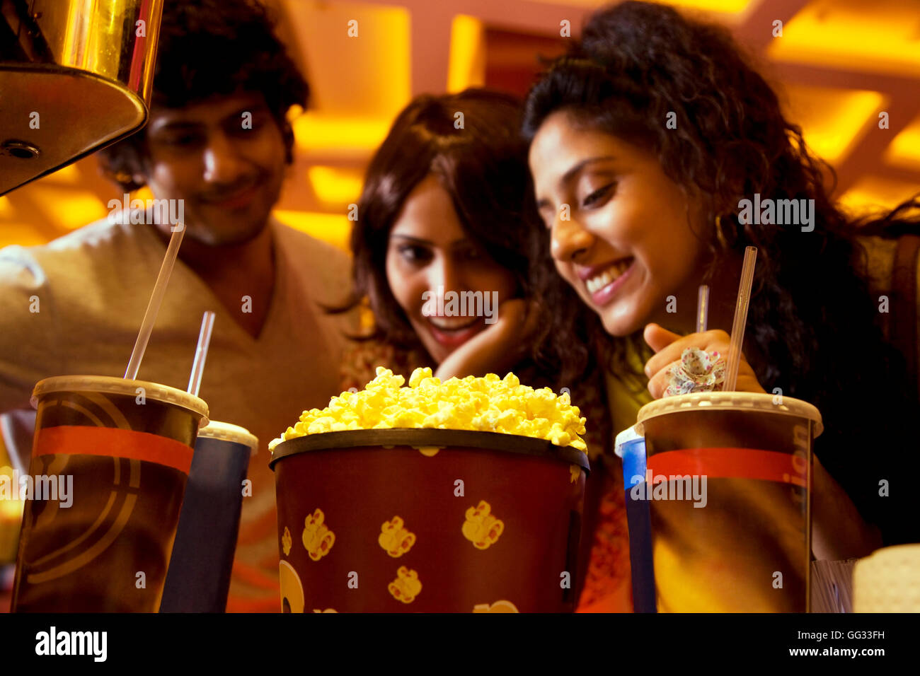 Happy friends looking at popcorn and soft drink Stock Photo - Alamy