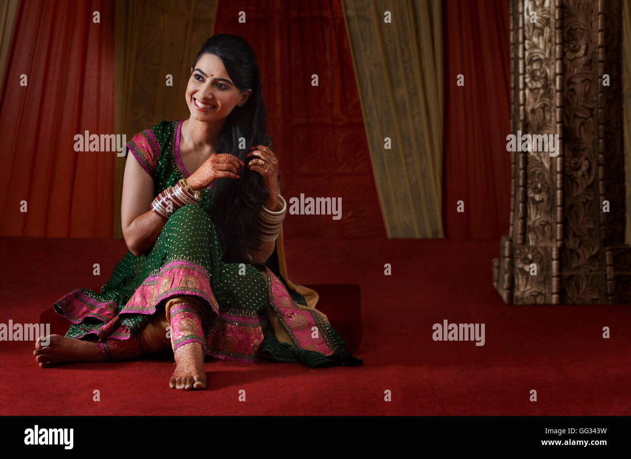 Full length of smiling Indian bride sitting while looking away Stock ...