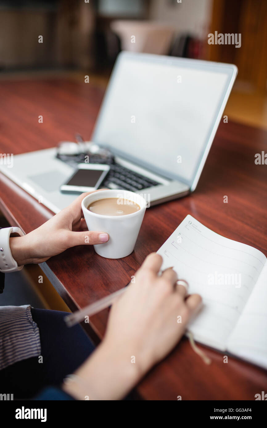 Woman writing in book while having tea Stock Photo - Alamy