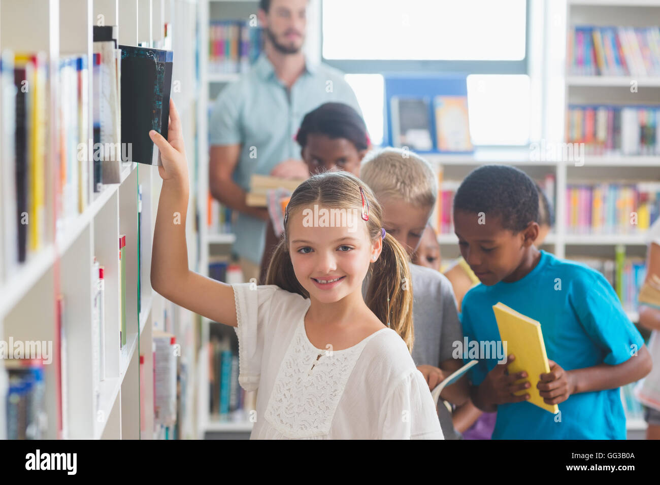 Smiling girl removing book from bookshelf in library Stock Photo - Alamy