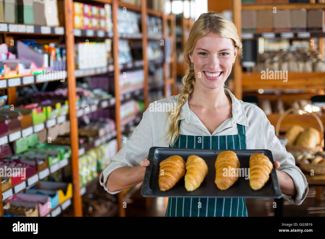 Smiling female staff holding tray of croissants in supermarket Stock ...